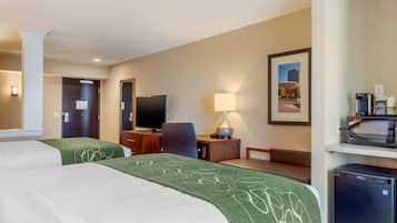 Quarto de hotel com duas camas, uma escrivaninha, televisão, luminária, refrigerador e um quadro na parede.