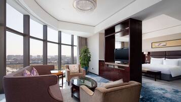 Quarto de hotel com uma janela grande, televisão, cama e área de estar com uma mesa de centro.