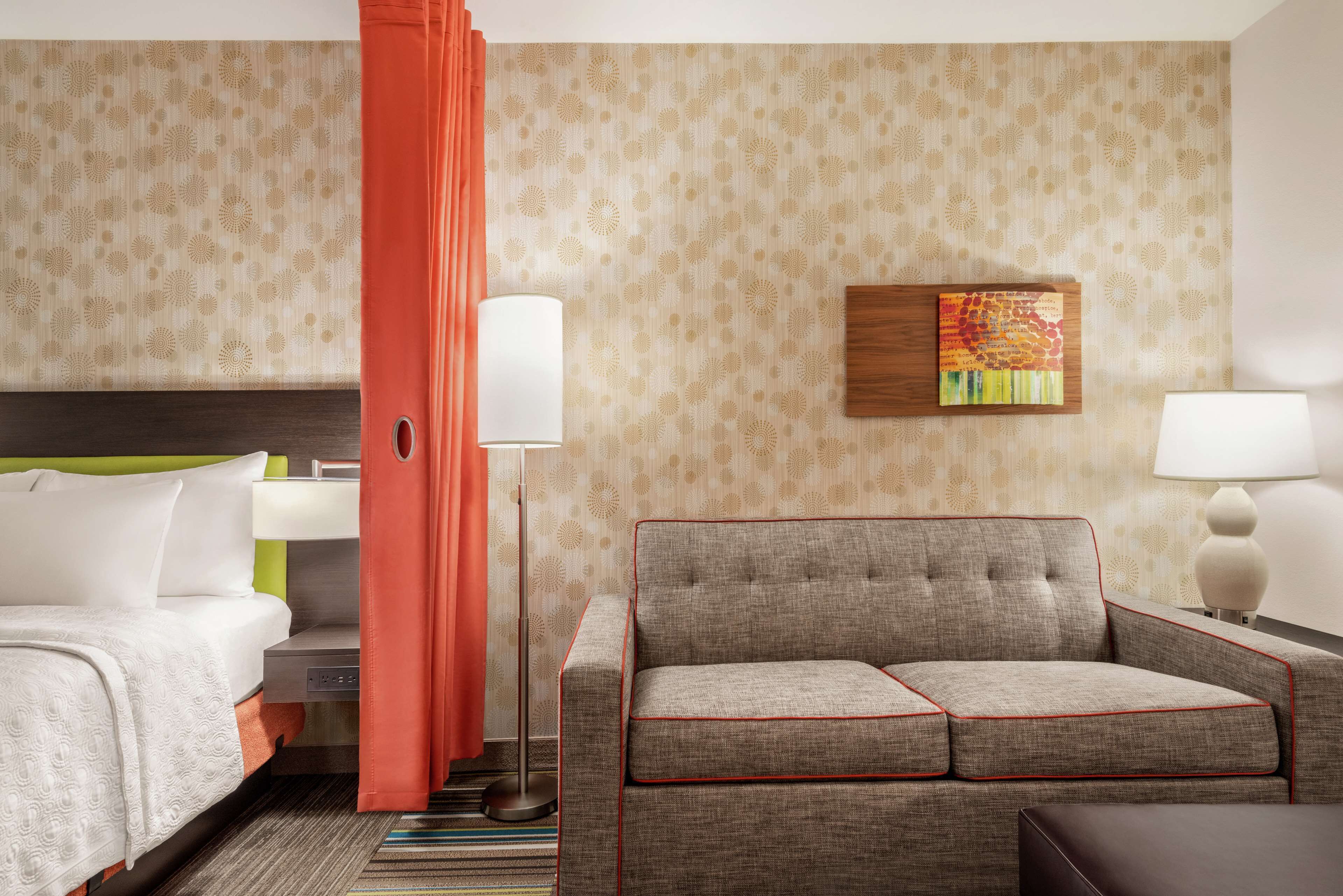 Quarto de hotel com cama, sofá, abajur e um quadro na parede.