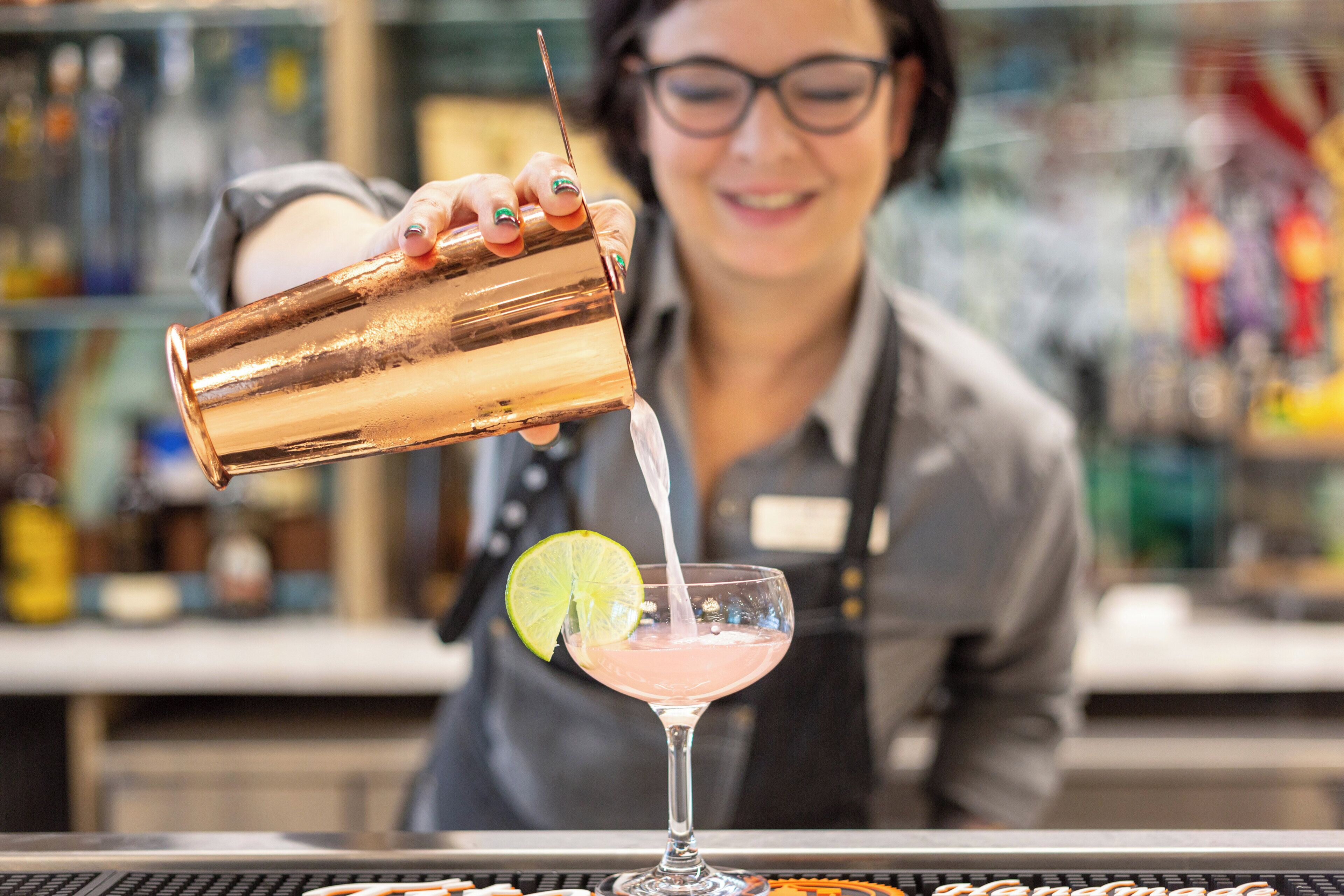 Um bartender servindo uma bebida em um copo, com uma fatia de limão.