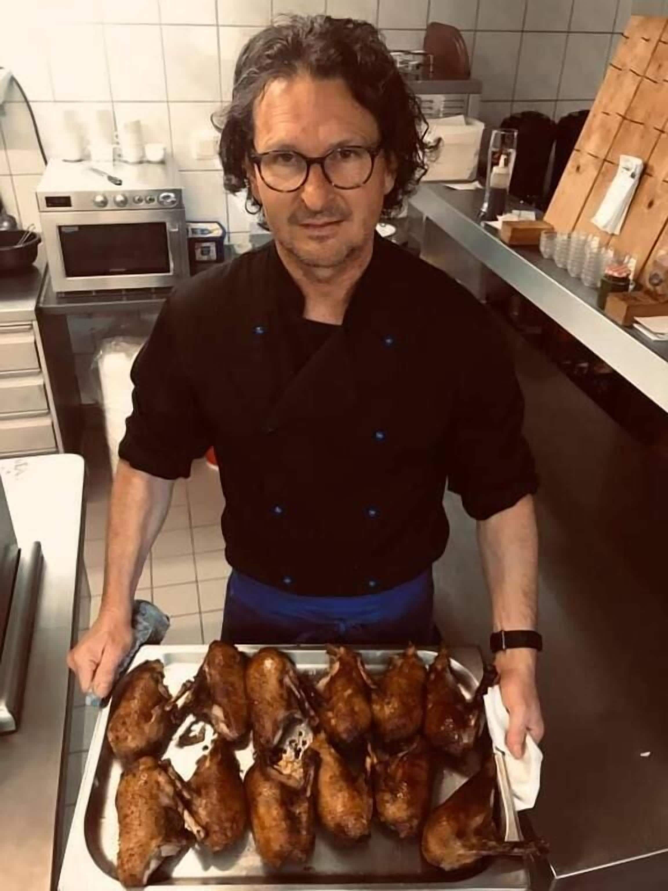 Uma pessoa segurando uma bandeja com frangos assados em uma cozinha.