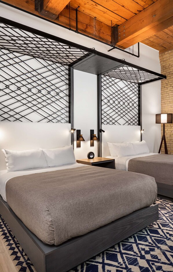 Quarto de hotel moderno com duas camas, um tapete estampado e um design de teto singular.