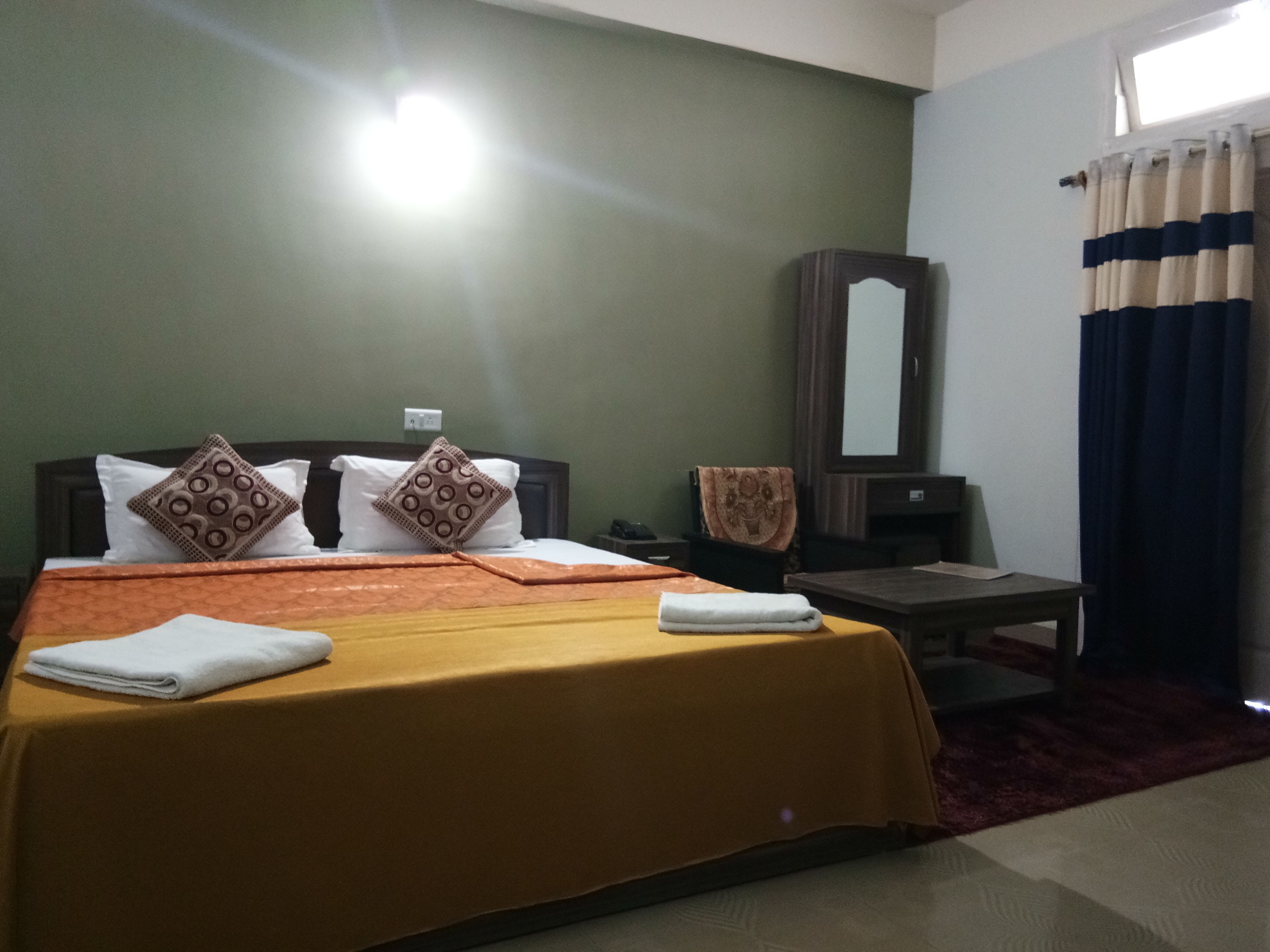 Quarto de hotel com cama, mesa de cabeceira, espelho e janela com cortinas.