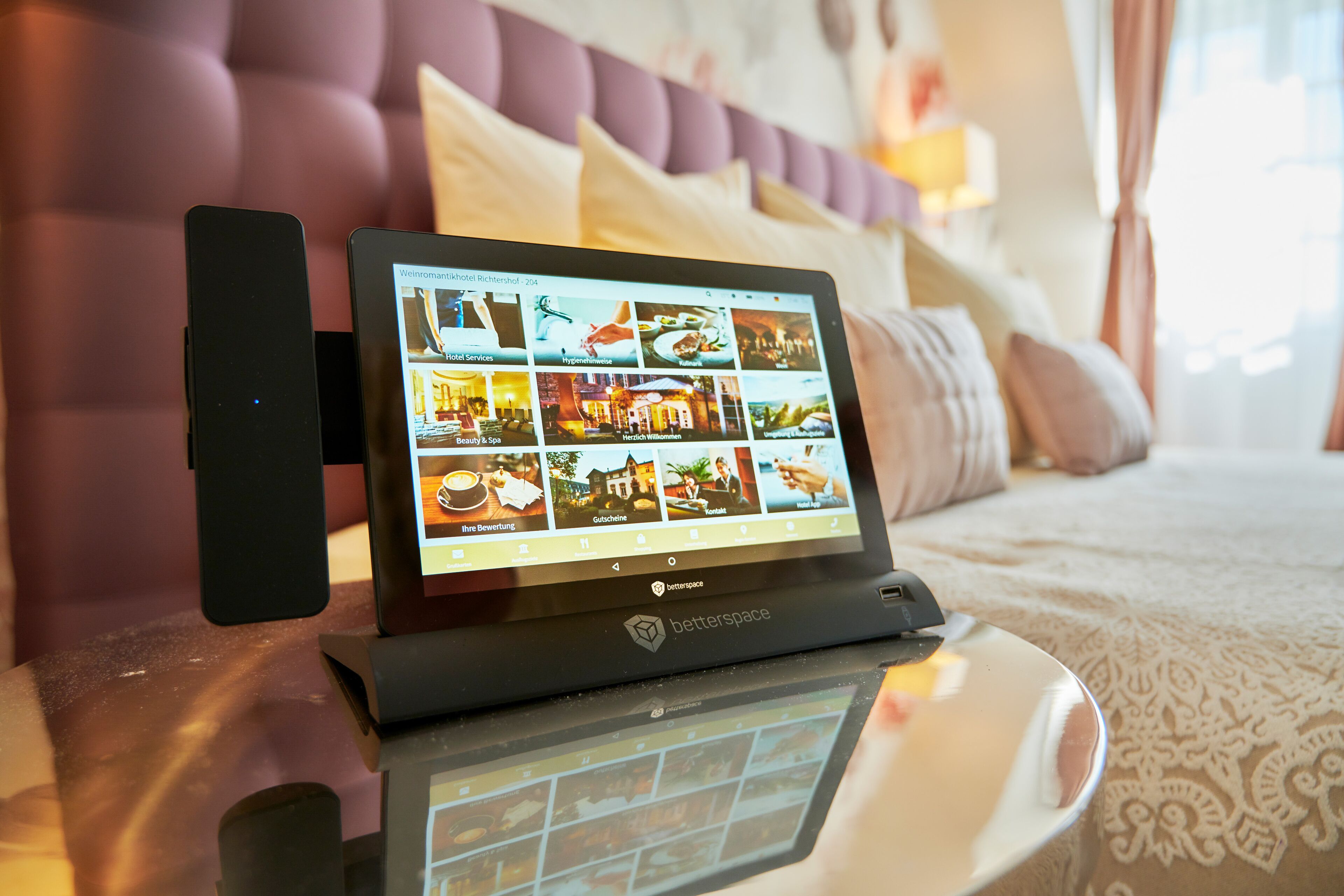 Um tablet exibindo o site de um hotel sobre uma mesa de cabeceira em um quarto de hotel.