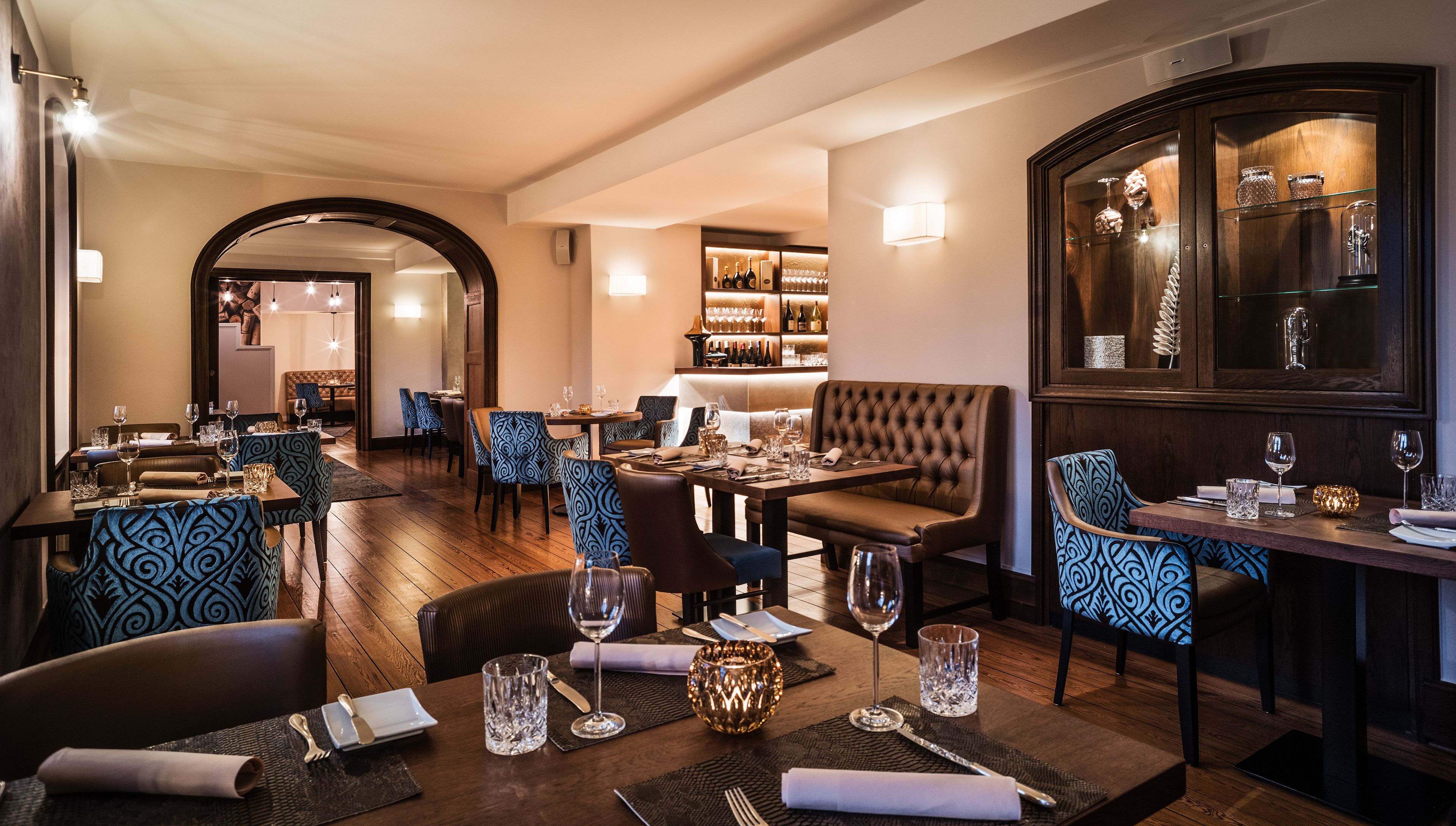Interior de restaurante com piso de madeira, cadeiras estampadas e mesas preparadas para refeições.