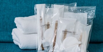 Conjunto de toalhas de algodão brancas e artigos de conjunto de algodão em sacos plásticos transparentes sobre uma superfície azul-turquesa.