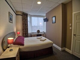 Quarto de hotel com cama, abajur, penteadeira, cômoda e janela com cortinas.
