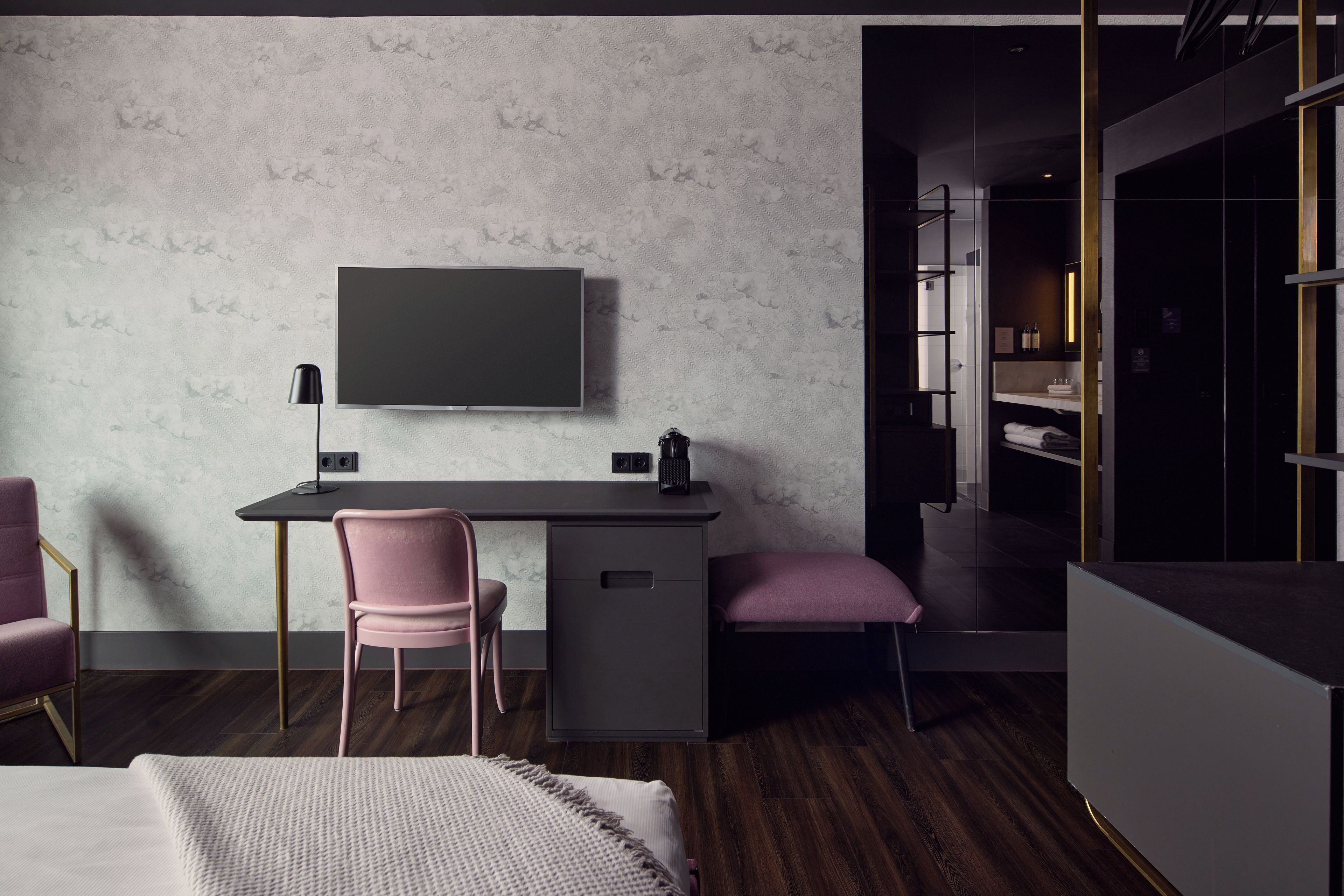 Quarto moderno com cama, escrivaninha, cadeira e televisão na parede.