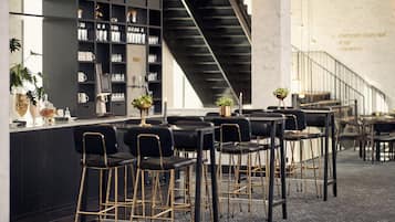 Uma área de bar moderna com banquetas pretas, um balcão com copos e uma escada ao fundo.