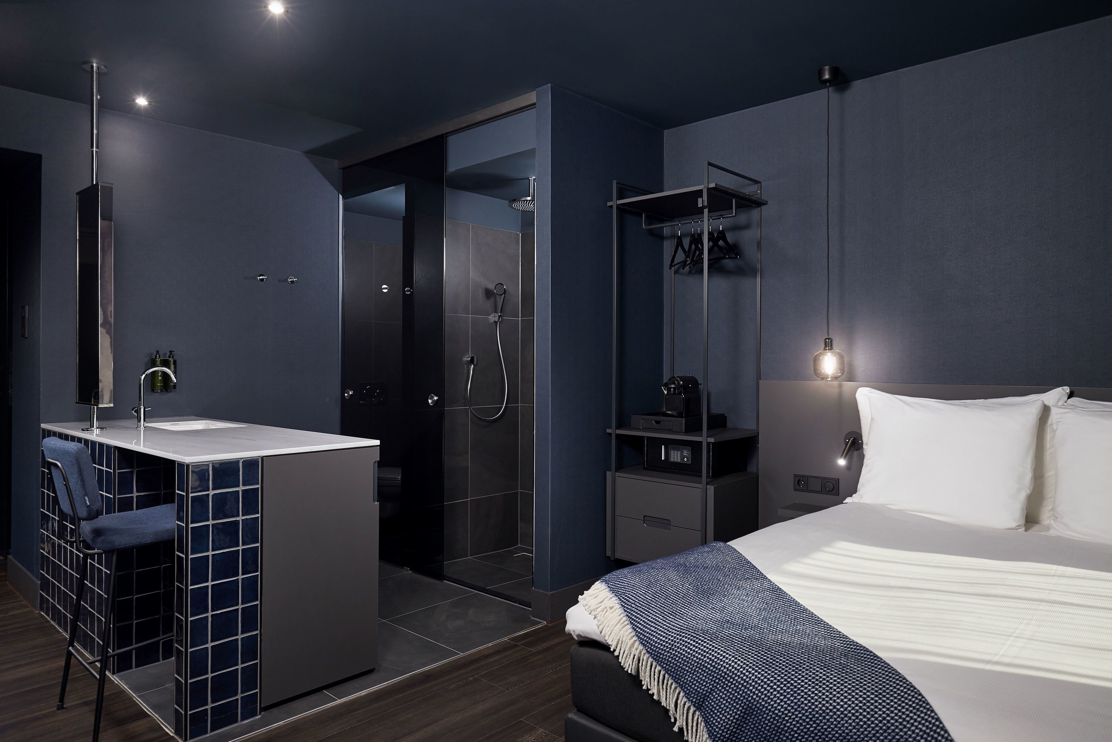 Quarto de hotel moderno com uma cama grande, uma escrivaninha embutida com pia, área de chuveiro e um guarda-roupa.