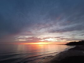 Uma praia ao pôr do sol, com águas calmas refletindo o céu.
