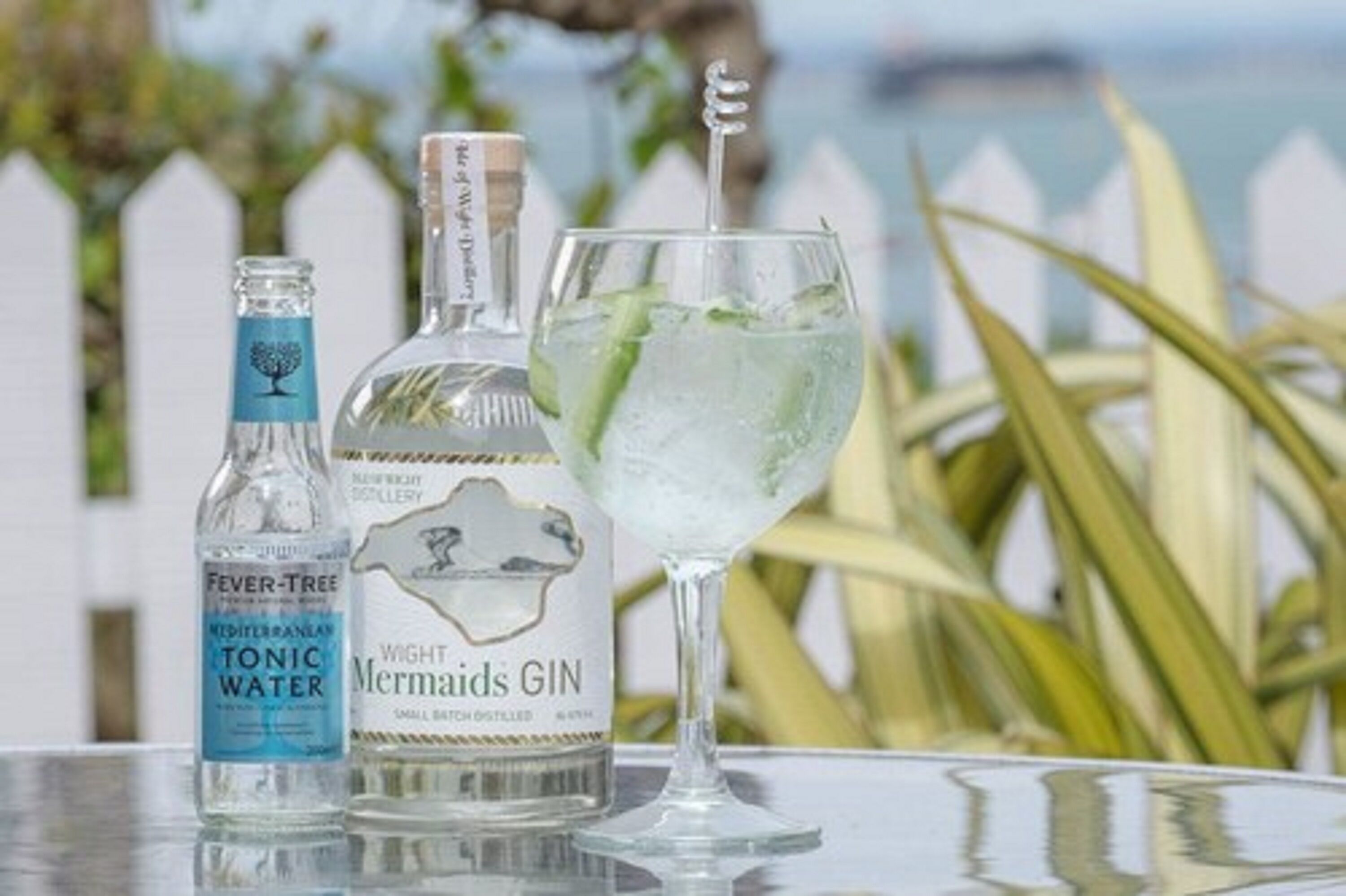 Uma garrafa de água tônica Mediterrânea Fever-Tree e um copo de gin Wight's com um ramo de hortelã sobre uma mesa.