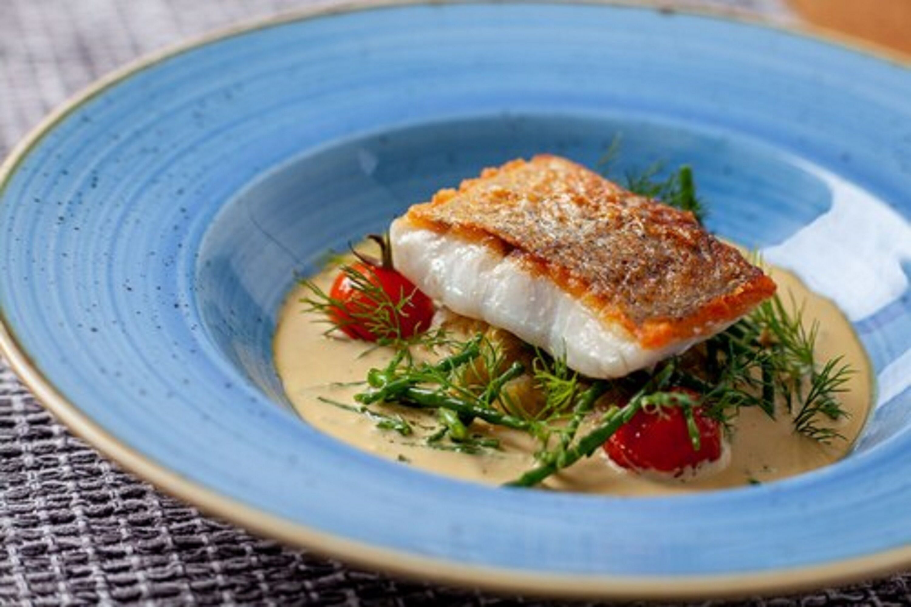 Prato com um pedaço de peixe, tomate cereja e ervas.
