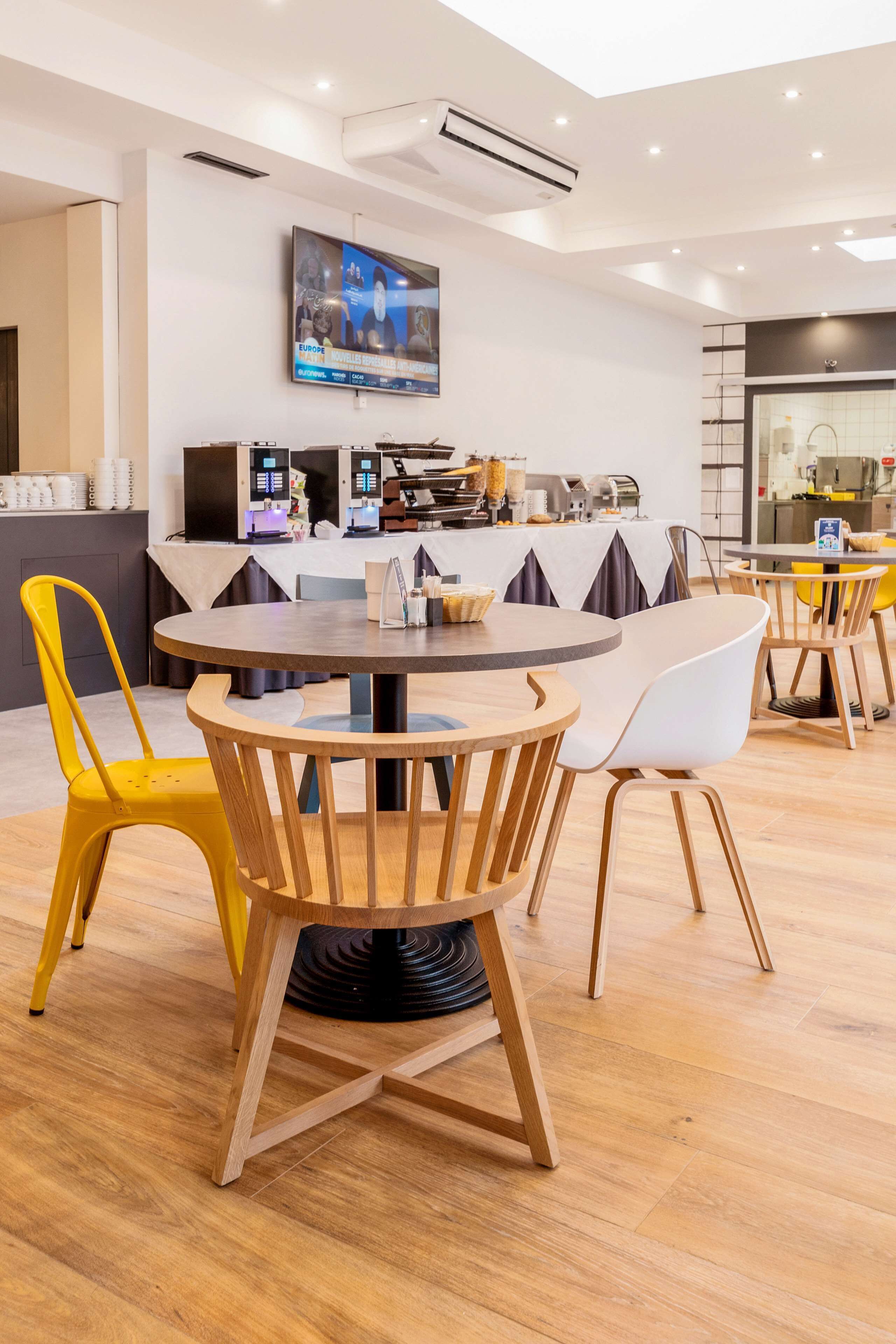 Uma área de refeições moderna com uma mesa redonda e cadeiras, uma cozinha ao fundo e uma televisão fixada na parede.