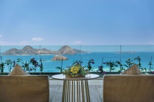 Uma mesa redonda com um arranjo floral, duas cadeiras marrons e vista para o mar e montanhas.