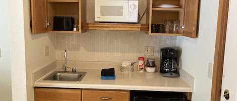 Cozinha compacta com armários de madeira, micro-ondas, máquina de café e lava-louças.