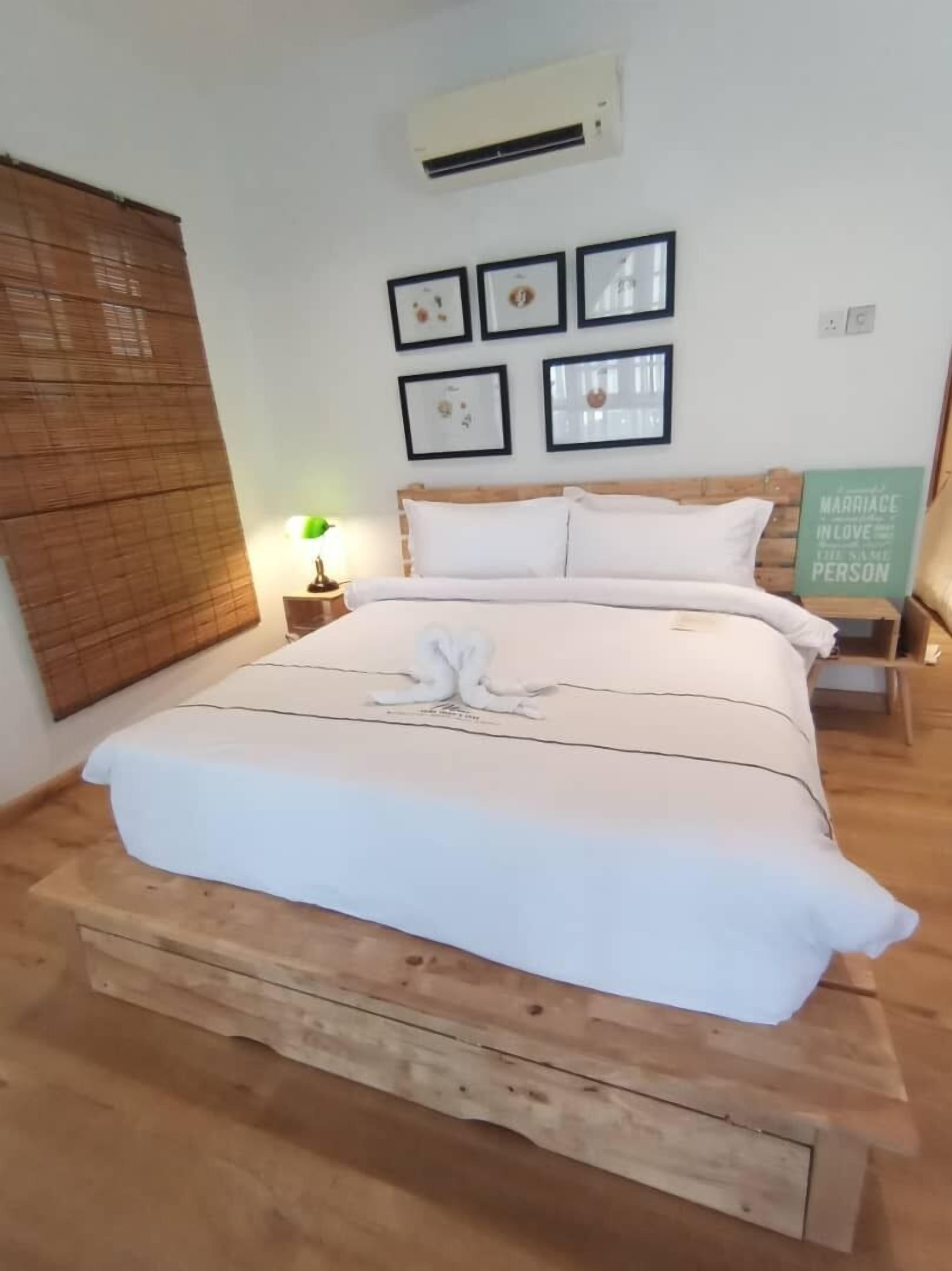 Quarto com cama, ar condicionado fixado na parede, quadros emoldurados, mesa de cabeceira com abajur e uma placa.