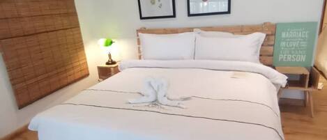 Quarto com cama, ar condicionado fixado na parede, quadros emoldurados, mesa de cabeceira com abajur e uma placa.