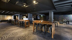 Um espaço amplo de bar com banquetas altas, balcão de madeira e tapete estampado.