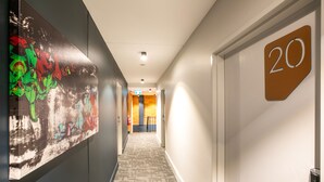 Um corredor com piso carpetado, uma placa na parede com o número 20 e uma pintura abstrata colorida à esquerda.