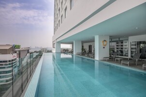 Piscina interior moderna com água azul cristalina, rodeada por um guarda-corpo de vidro e espreguiçadeiras.