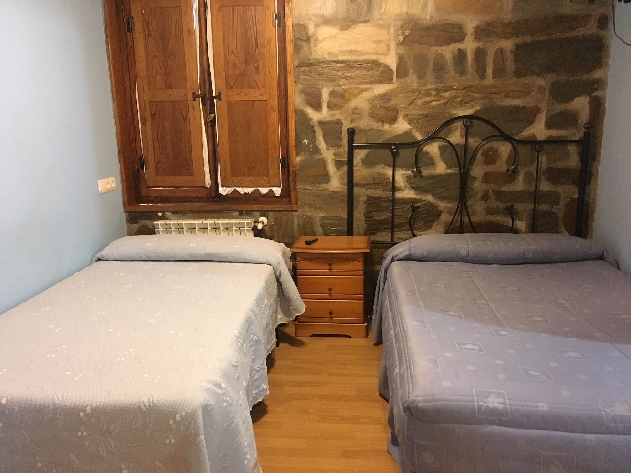 Um quarto pequeno e aconchegante com duas camas de solteiro, cômoda de madeira e parede de pedra.