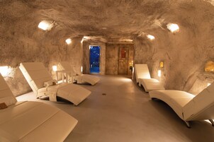 Um quarto de spa com cadeiras reclináveis brancas, parede de pedra e uma porta que dá para outra área.