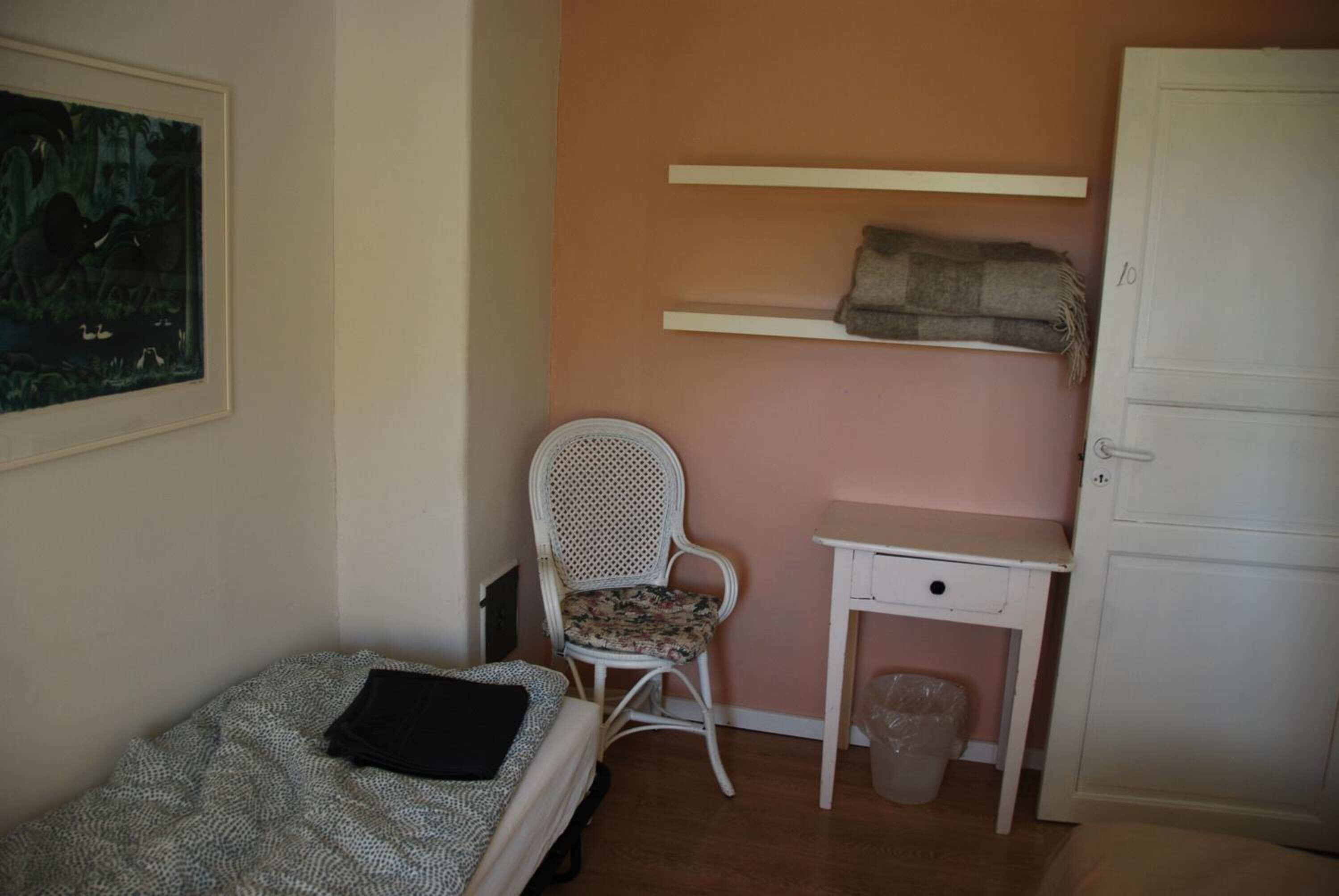 Quarto pequeno com cama, cadeira, escrivaninha e porta.