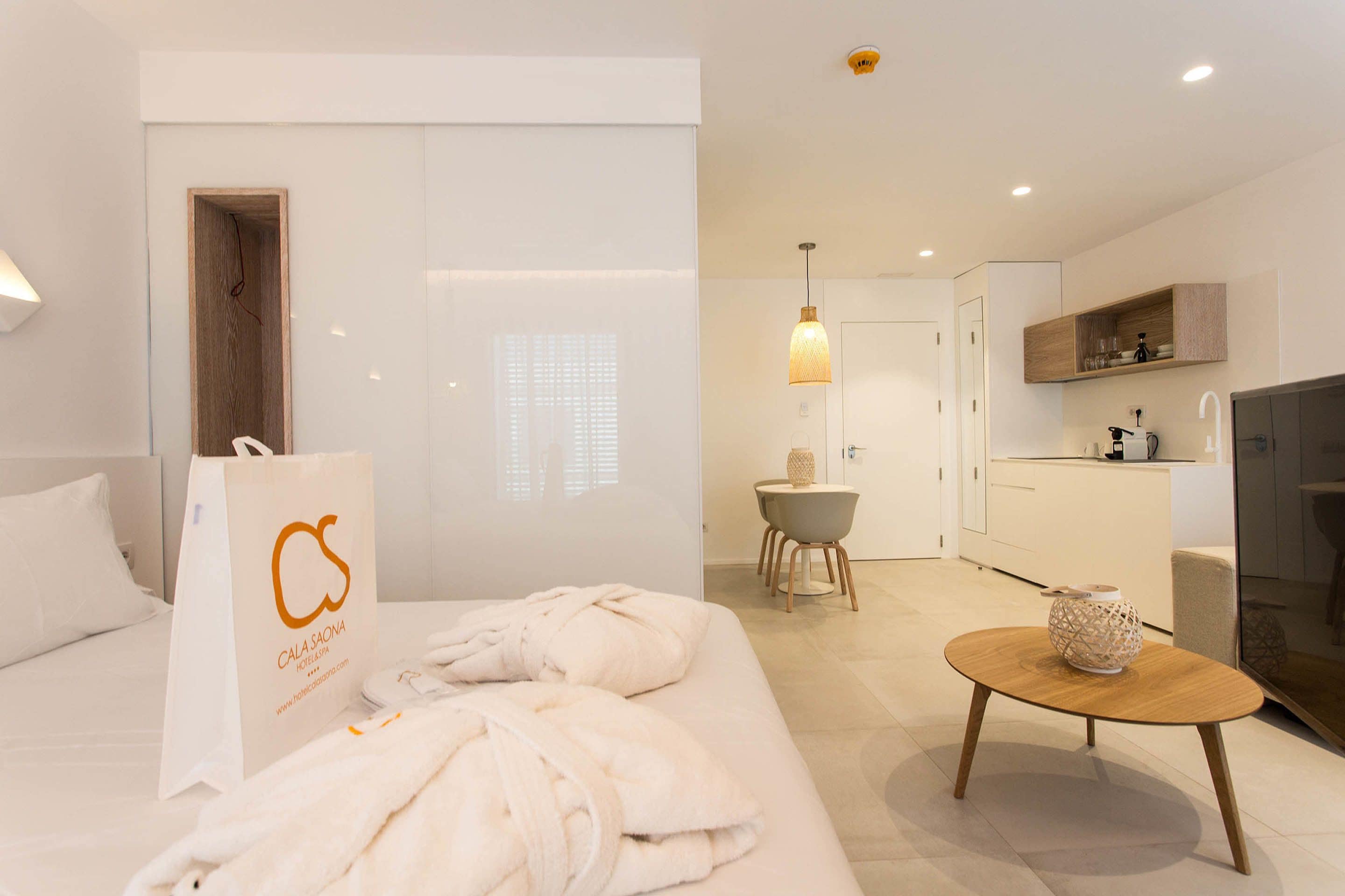 Quarto de hotel moderno com uma cama, uma mesa de madeira, um pequeno espaço de refeições e uma cozinha.