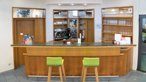 Uma área de bar com balcão, dois banquetes verdes e prateleiras com copos e taças.