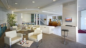 Um lobby moderno com mobiliário branco, um balcão de recepção e uma escadaria que leva a outro andar.