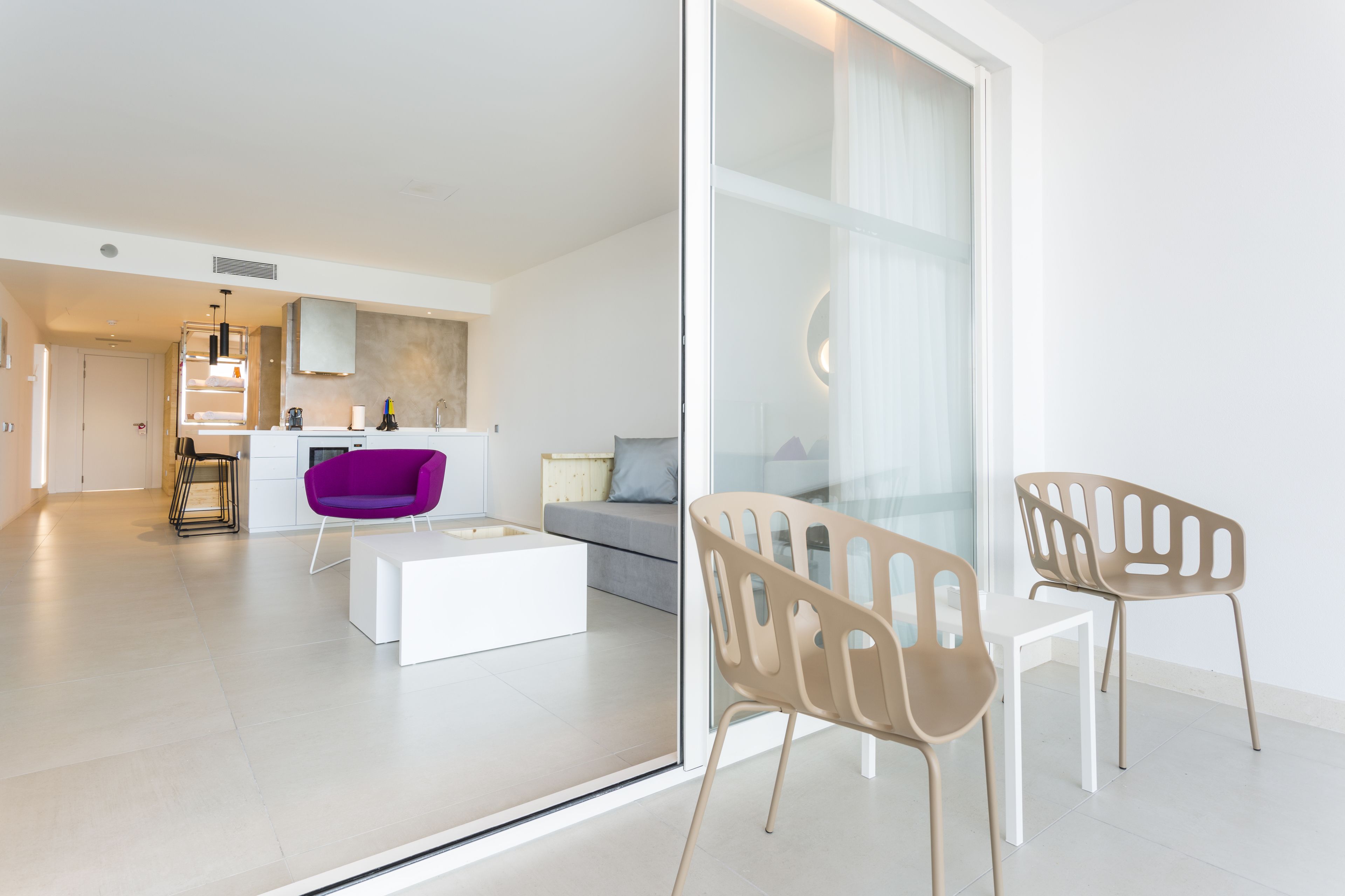 Uma sala de estar moderna com um sofá branco, uma poltrona roxa e duas poltronas bege.