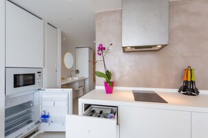 Uma cozinha moderna com micro-ondas embutido, geladeira com dispensador de água, uma orquídea rosa e um conjunto de utensílios de cozinha coloridos no balcão.