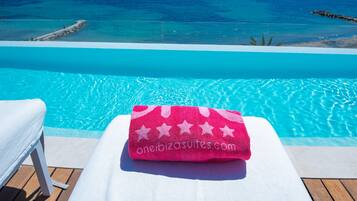Vista da piscina com uma toalha rosa em uma espreguiçadeira, água azul cristalina e formações rochosas ao longe.