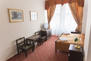 Quarto de hotel com cama, escrivaninha, cadeira, televisão e duas molduras na parede.