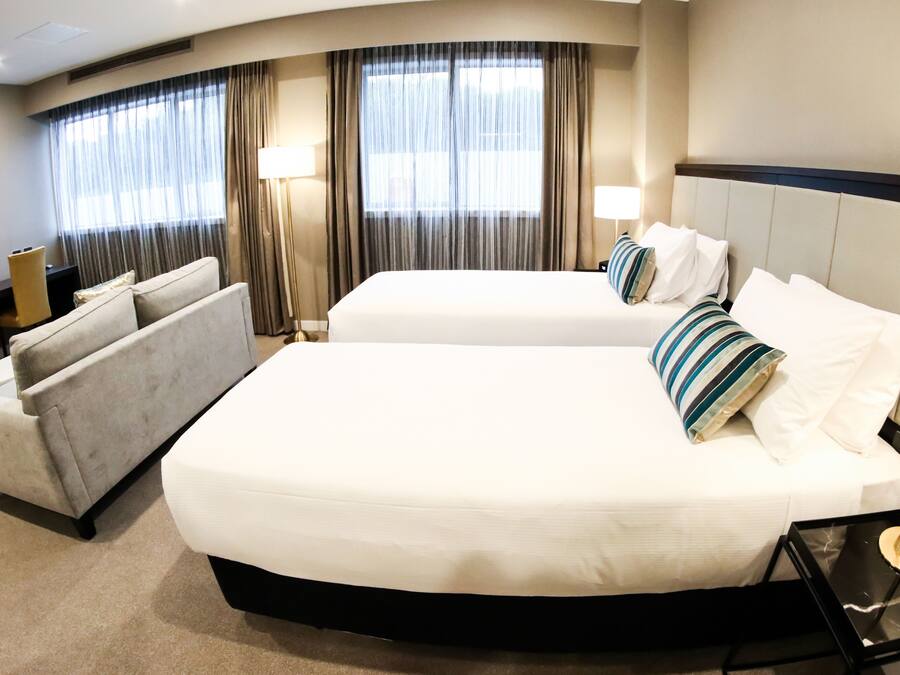 Quarto de hotel com duas camas, um sofá e uma escrivaninha com abajur.