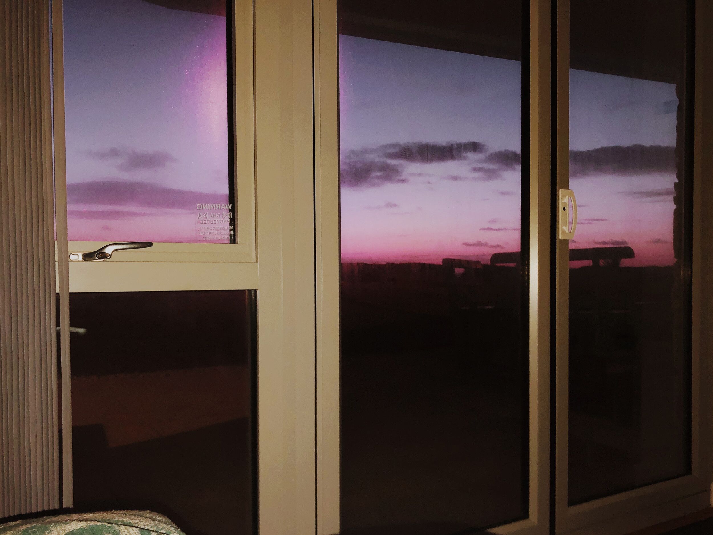 Janela com vista para um pôr do sol e um banco lá fora.