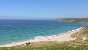 Uma praia costeira com vista clara do oceano, areal arenoso e terreno coberto de relva.