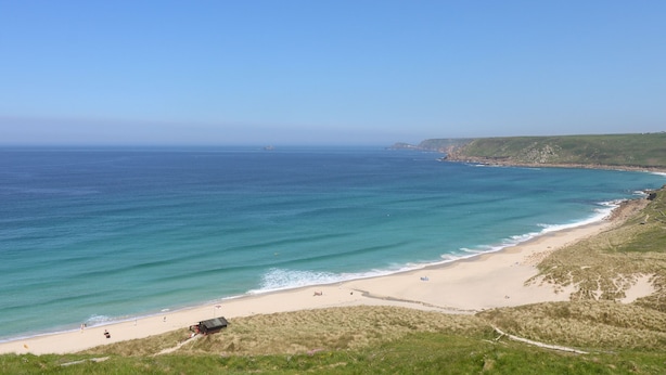 Uma praia costeira com vista clara do oceano, areal arenoso e terreno coberto de relva.