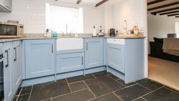 Uma cozinha moderna com armários azul-claros, piso de azulejos pretos, micro-ondas embutido e uma janela com persianas.