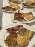 Uma mesa com diversos itens de café da manhã, como hash browns, bacon, ovos e biscoitos.