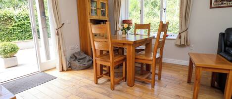 Uma sala de jantar com mesa e cadeiras de madeira, um armário com portas de vidro e vista para o verde lá fora.