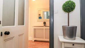 Um corredor com uma porta branca, um tapete marrom, uma planta em vaso e uma pequena mesa com uma gaveta.