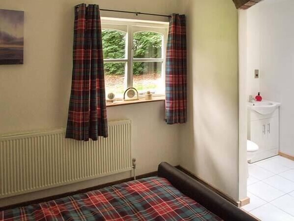 Um quarto com cama, janela com cortinas, radiador e banheiro com pia.
