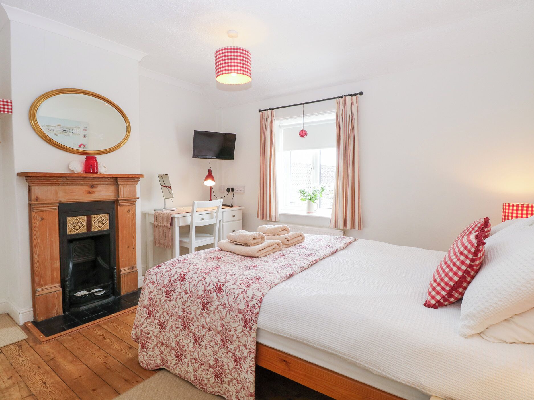 Quarto com cama, escrivaninha, lareira, televisão e janela com cortinas.
