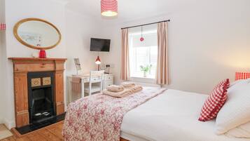 Quarto com cama, escrivaninha, lareira, televisão e janela com cortinas.