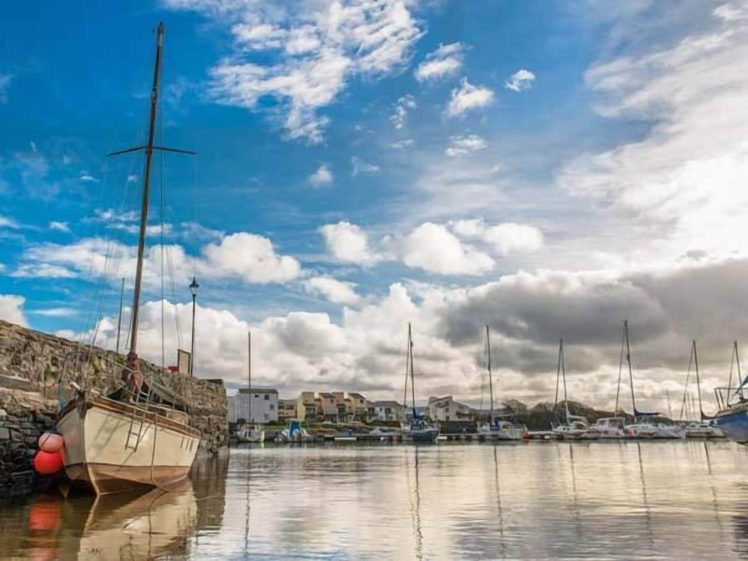 Um porto com barcos atracados, uma parede de pedra e edifícios ao fundo.