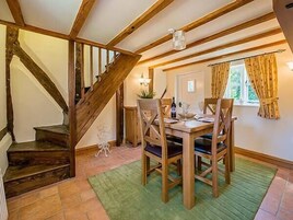 Uma área de refeições com mesa e cadeiras de madeira, uma escada e uma janela com cortinas.