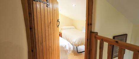 Quarto com guarda-roupa de madeira, cama com roupa de cama branca e uma pequena mesa de cabeceira.