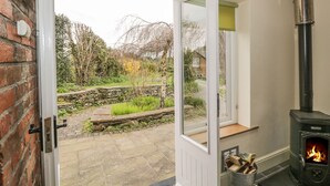 Quarto com parede de pedra, porta de madeira, janela com vista para um jardim e lareira a lenha.